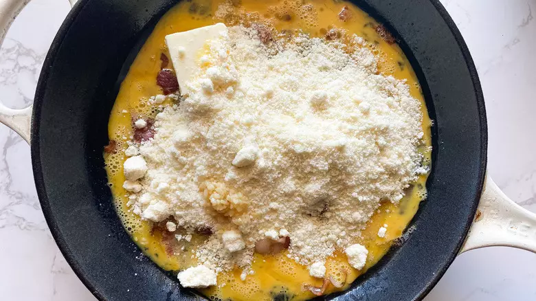 Akwa, anụ ezi esiri esi, bọta, na cheese parmesan grated na skillet.