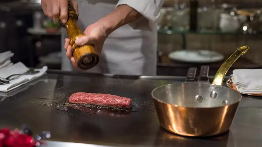 a man do chef moendo sal sobre a carne de vaca kobe na prancha na cociña