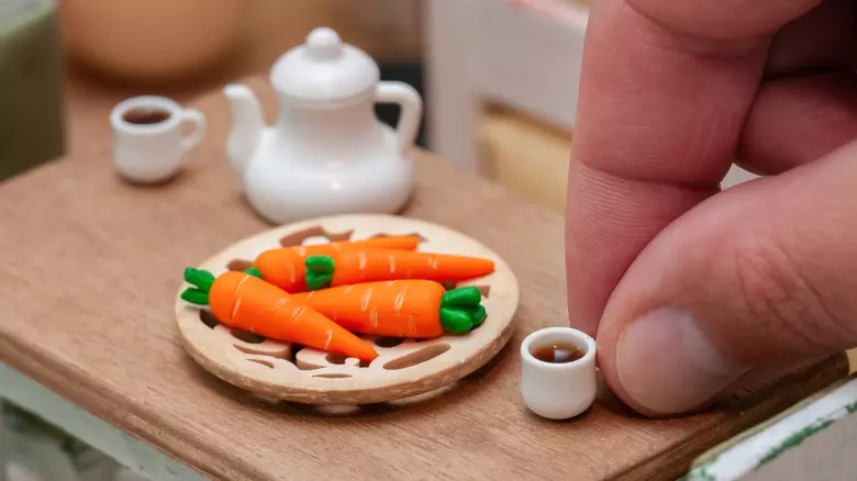 tangan nyekel cangkir kopi cilik ing jejere wortel cilik