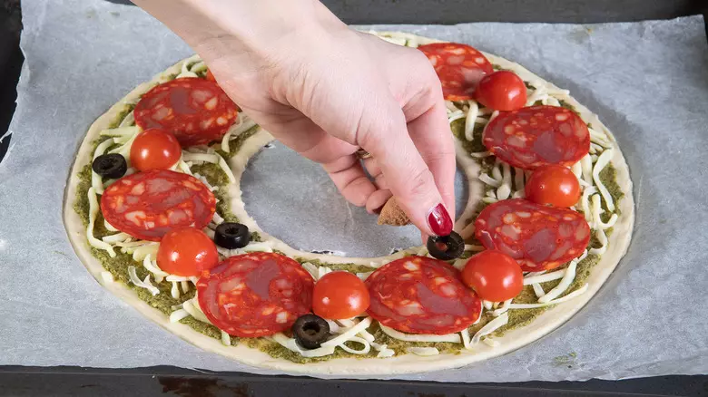 ręka nakładająca oliwkę na pizzę