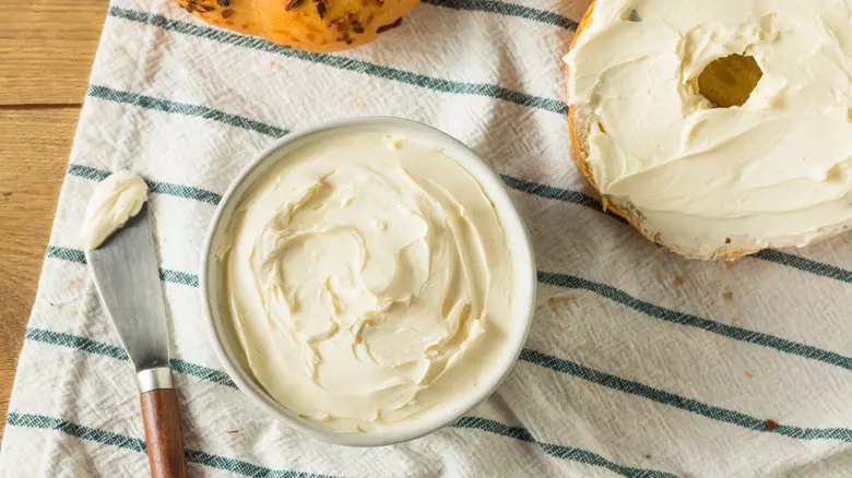 Tina de queso crema sobre una toalla a rayas con un cuchillo para untar