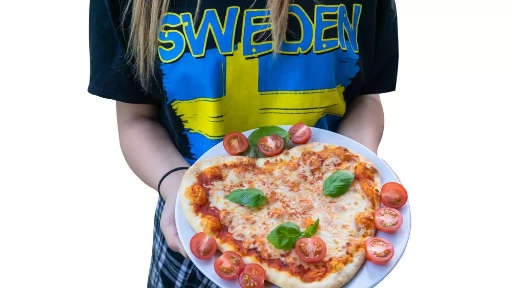 Persoon die een T-shirt met Zweedse vlag draagt en pizza vasthoudt