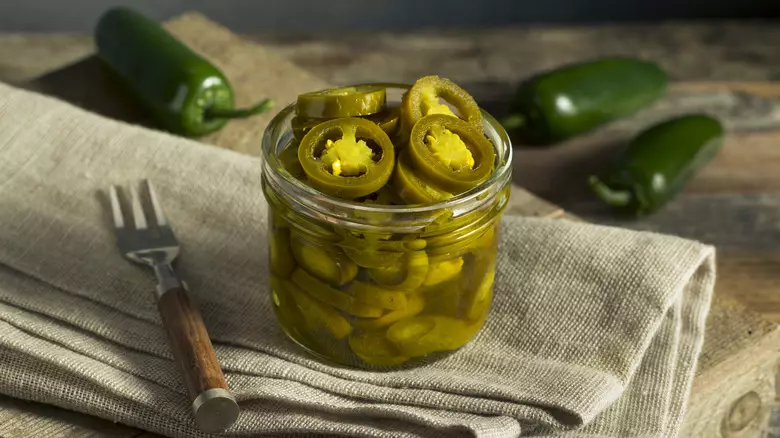 Kavanoz me jalapeños turshi i rrethuar nga speca të freskët dhe të plotë jalapeño