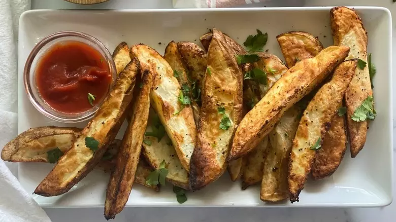 steak fries ເທິງຈານທີ່ມີ ketchup ໂຖປັດສະວະຂະຫນາດນ້ອຍ.