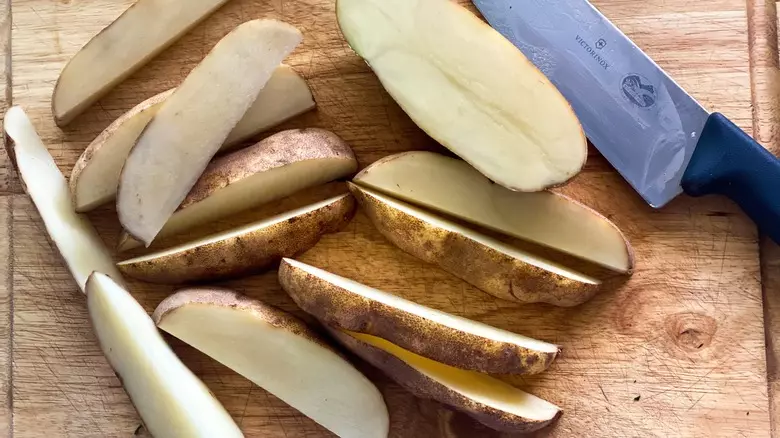 Patate a fette su un tagliere con un coltello.