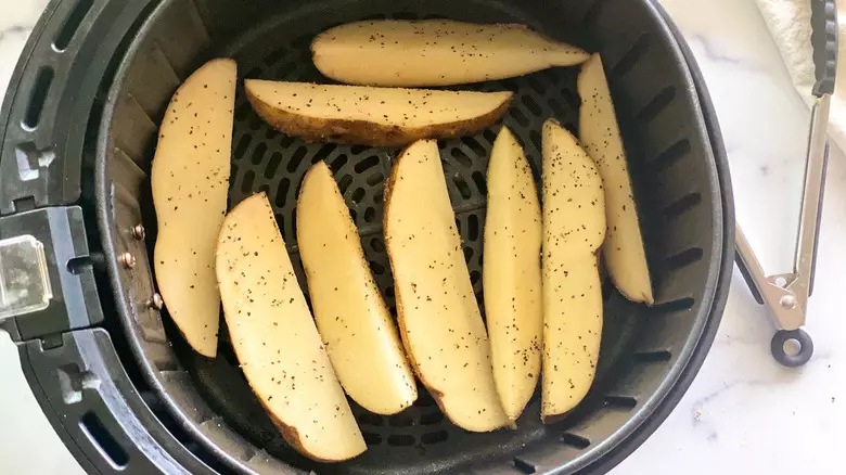 Potato wedges pleatst yn in luchtfryer koer.