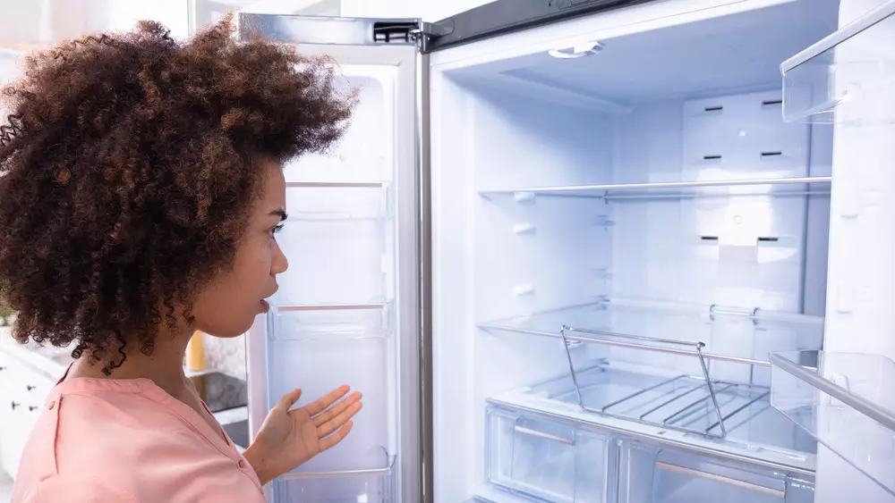 Babaeng nakatingin sa walang laman na refrigerator