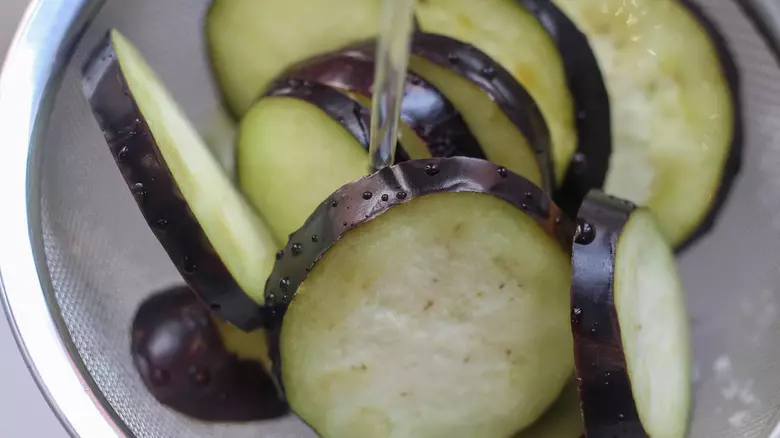 Aubergineskiver i et dørslag og plassert under rennende vann.