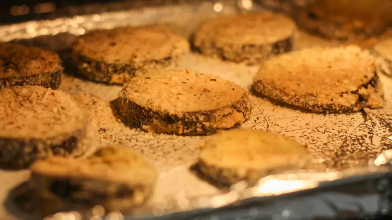 Panerte aubergineskiver på et foret stekebrett inne i ovnen.