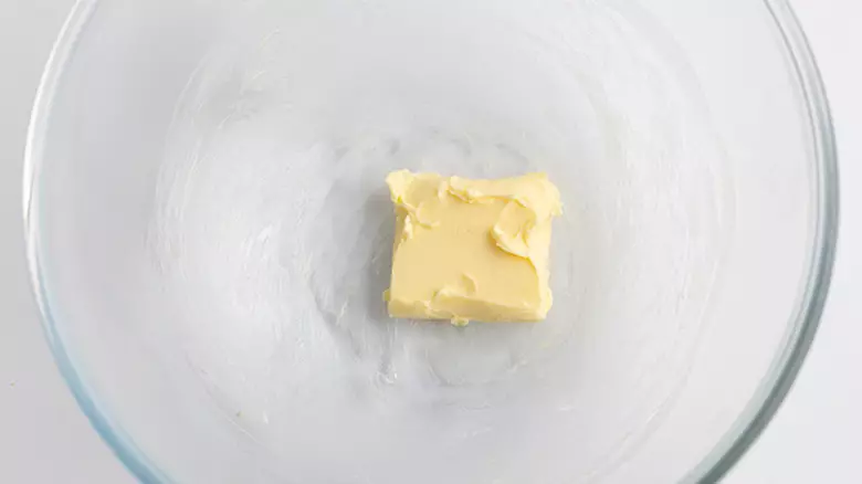 एक गिलास मिक्सिंग बाउल में मक्खन की एक थपकी का उपरि शॉट