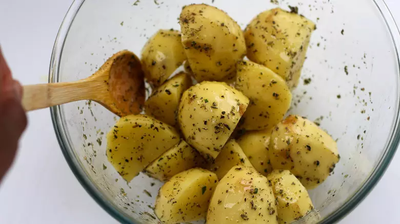 Gros plan d'une personne utilisant une cuillère en bois pour remuer les pommes de terre dans un bol transparent