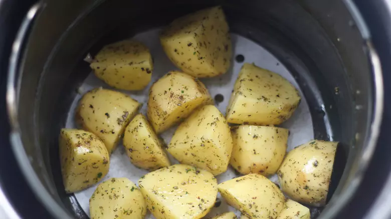 Pommes de terre crues hachées couvertes d'huile et d'épices assises dans une friteuse à air