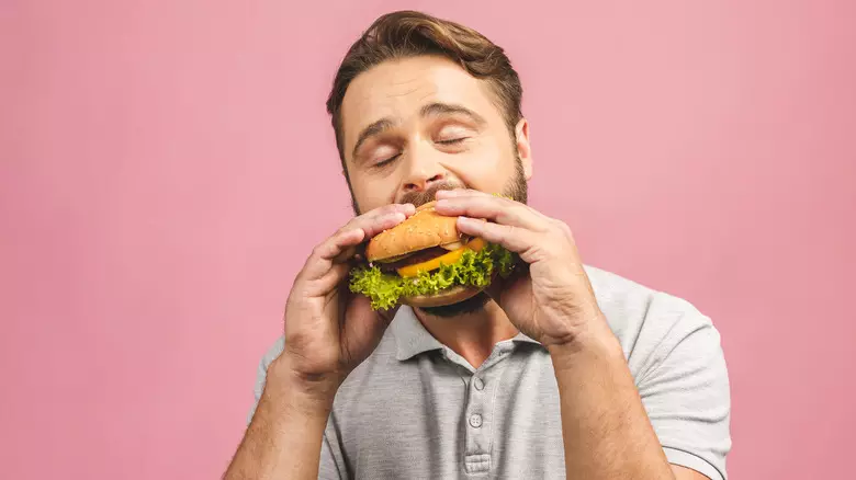 muž hryzie hamburger na ružovom pozadí