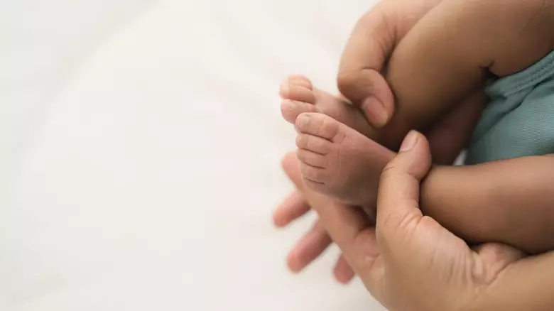 બાળકના પગ પુખ્ત વયના હાથ દ્વારા પકડવામાં આવે છે