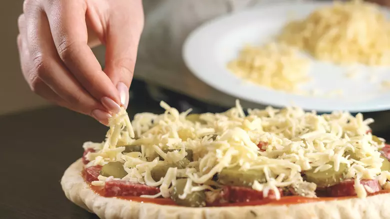 生のピザにチーズを加える手