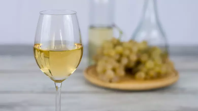 Чаша бяло вино с грозде на заден план