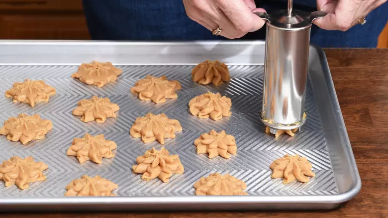 Biscoitos sendo espremidos através de uma prensa de biscoitos em uma assadeira