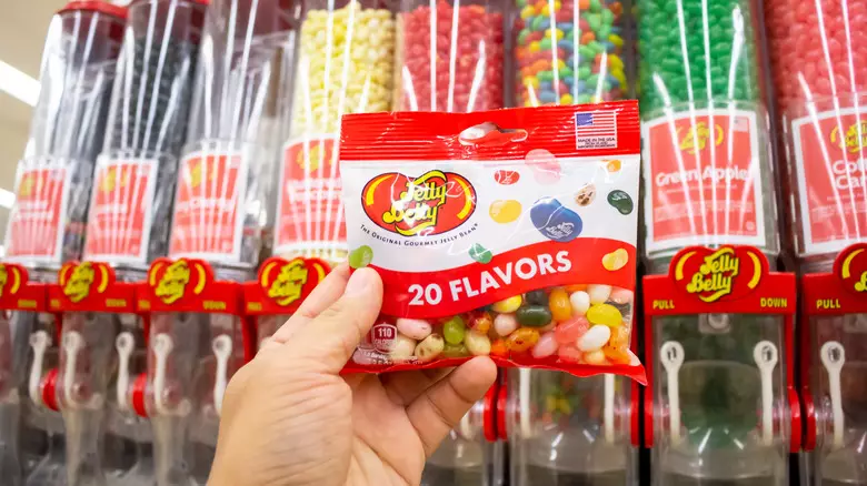 Диспенсерлердин алдында Jelly Belly пакетин кармап турган адам