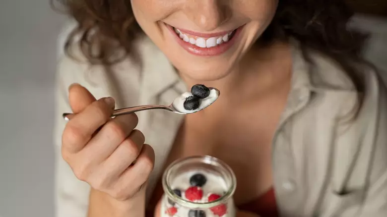 Улыбающийся человек ест йогурт с фруктами