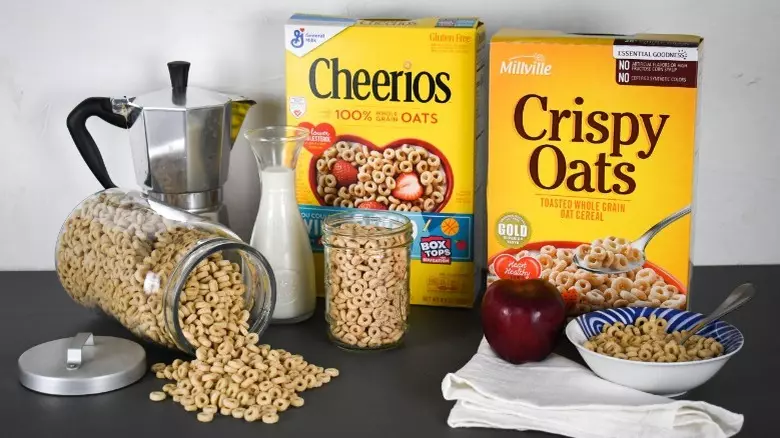 kotak sereal Cheerios dan oat renyah di atas meja sarapan dengan susu, kopi, apel