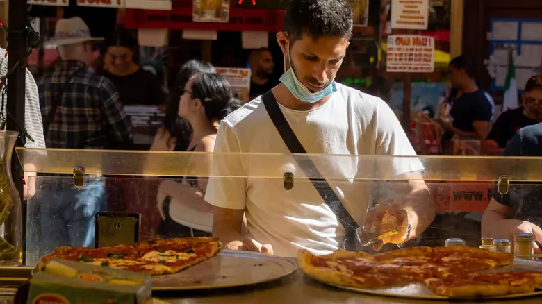 Un hombre poniendo aderezos en una pizza al estilo de Nueva York