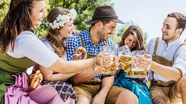 Minsken yn lederhosen en dirndl en bier steins