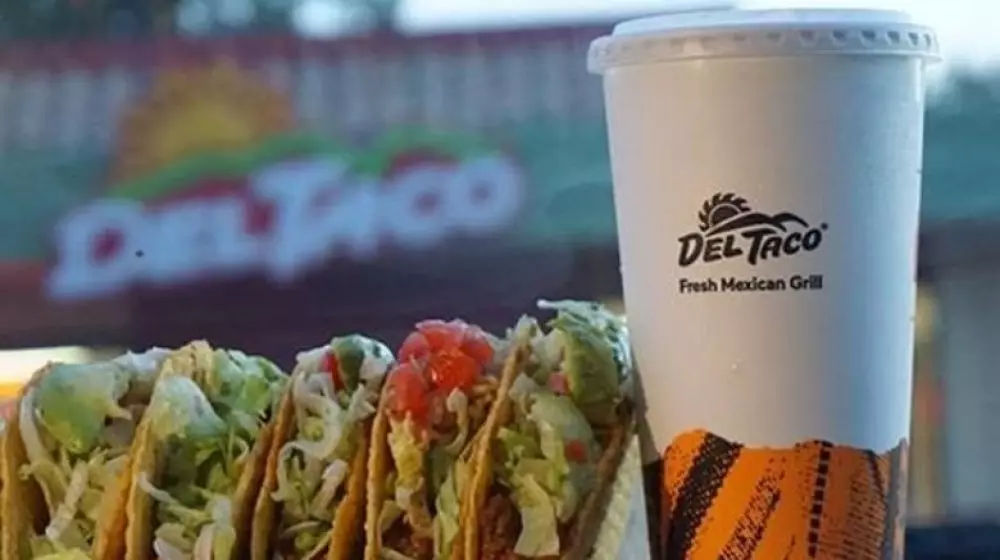 Tacos e bebida Del Taco cun restaurante ao fondo