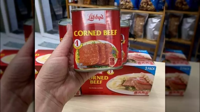 Valaki a kezében egy doboz Libby's Corned Beef tokkal az asztalon