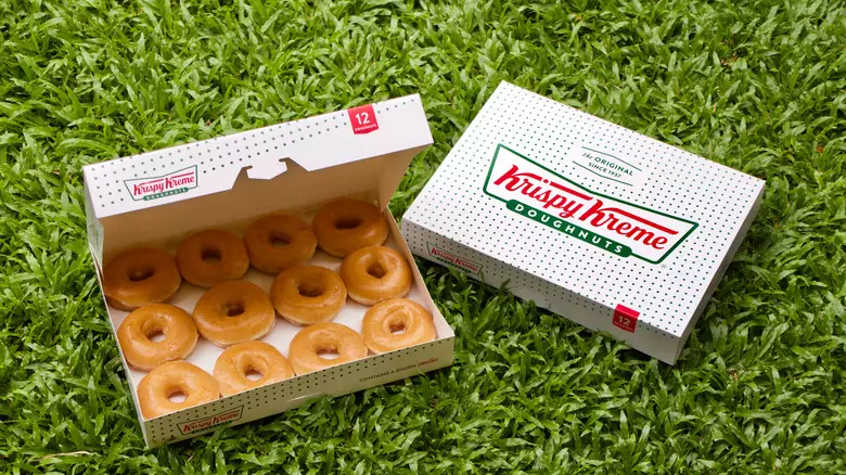 Закрита коробка та відкрита коробка пончиків Krispy Kreme на траві