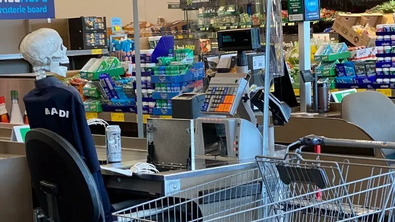 Kkeleton bilqiegħda fis-siġġu wara l-cash register f’Aldi