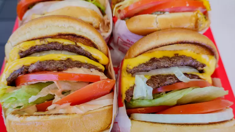 Detailní záběr na četné In-N-Out hamburgery se sýrem, hlávkovým salátem, cibulí a rajčaty