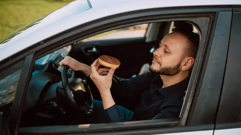 Home comendo unha rosca no seu coche