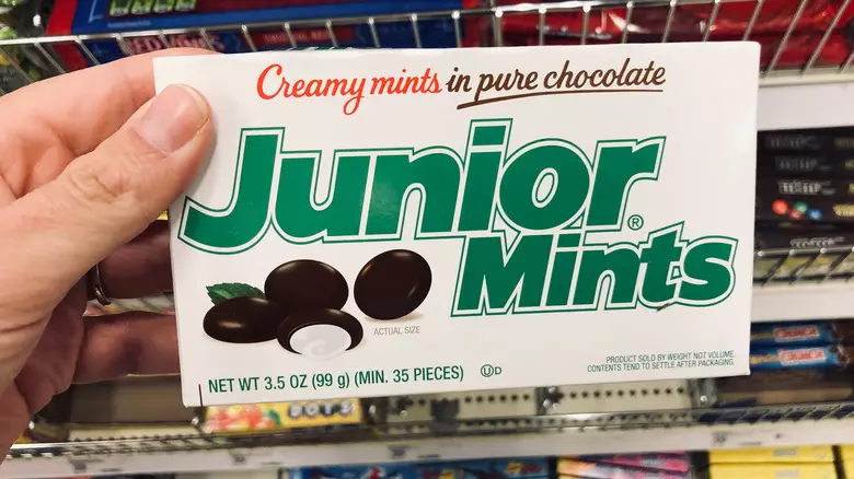 Kamot nga nagkupot sa kahon sa Junior Mints atubangan sa candy rack