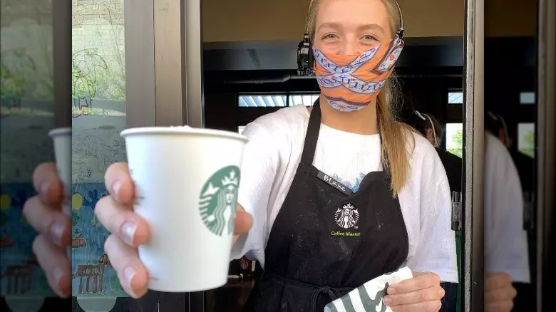 En maskert Starbucks-ansatt gir en drink gjennom drive-thru