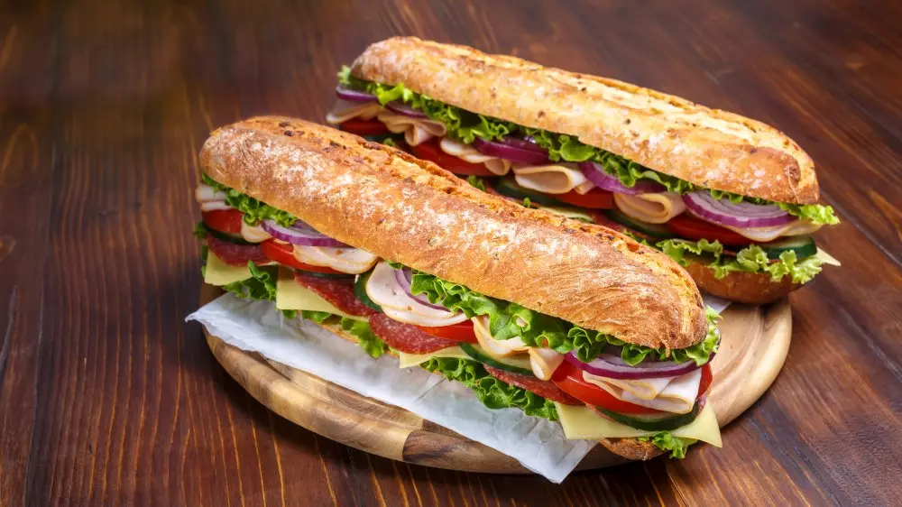 لکڑی کے پلیٹر پر دو ذیلی سینڈوچ