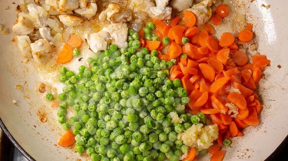 pois et carottes ajoutés à une poêle chaude pour riz frit au poulet