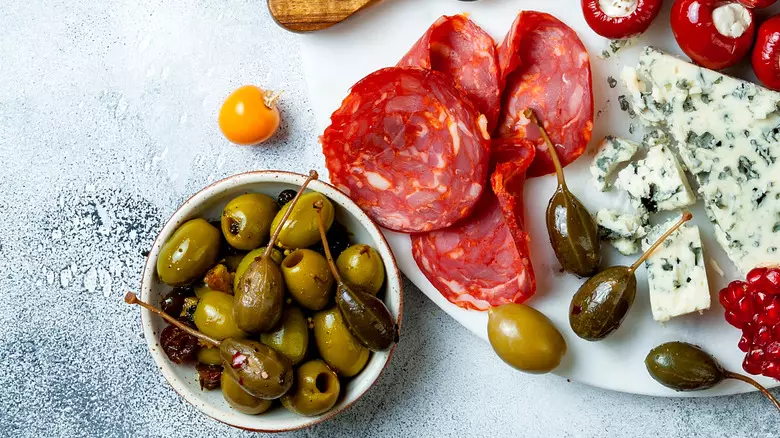 valge taldrik vorstiliha ja juustudega oliivide ja päikesekuivatatud tomatite ning kahe klaasi valge veiniga