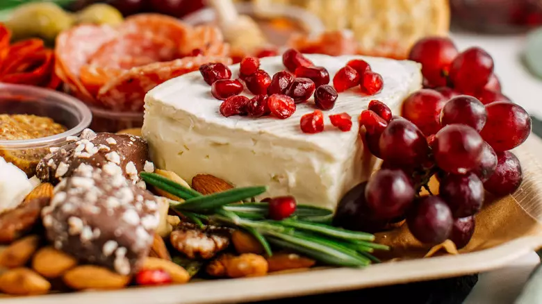 närbild av charkplatta med fokus på brie-klyfta garnerad med granatäpplekärnor och färsk rosmarinkvist