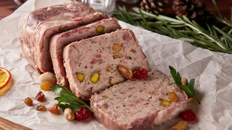 terrine yaing'ono yodulidwa pang'ono yokhala ndi pistachio pazikopa zoyera zopindika ndi cranberries zouma ndi zoumba ndi zitsamba zatsopano zokongoletsa