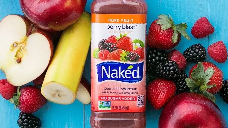 Naked Berry pudele, kas atrodas uz gaiši zilas virsmas, ko ieskauj augļi un ogas