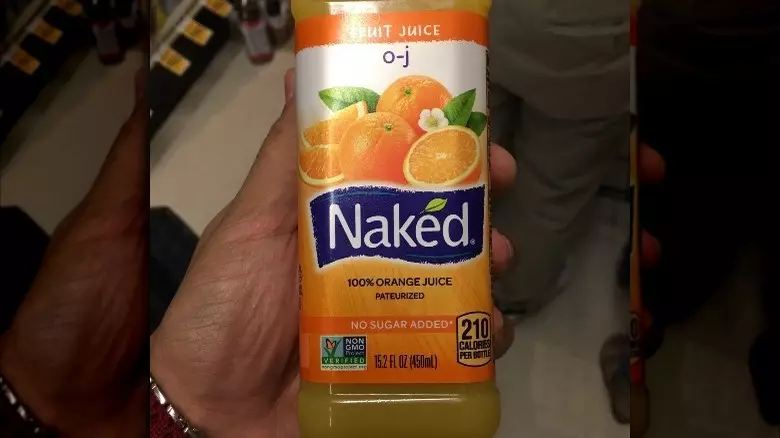 Usa ka kamot nga nagkupot sa usa ka baso nga botelya sa organge juice, nga adunay usa ka straw, atubangan sa usa ka orange nga backdrop