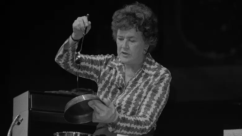 Julia Child cầm thìa và chảo trong bếp trên nền đen