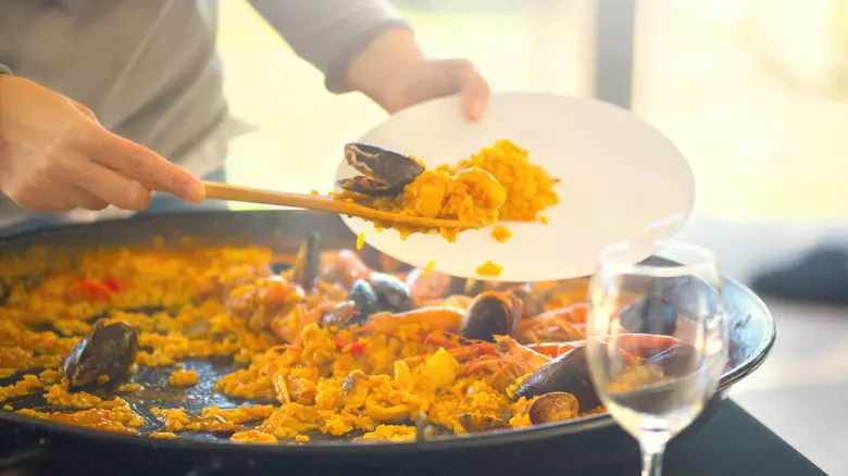 Una persona poniendo paella en un plato.