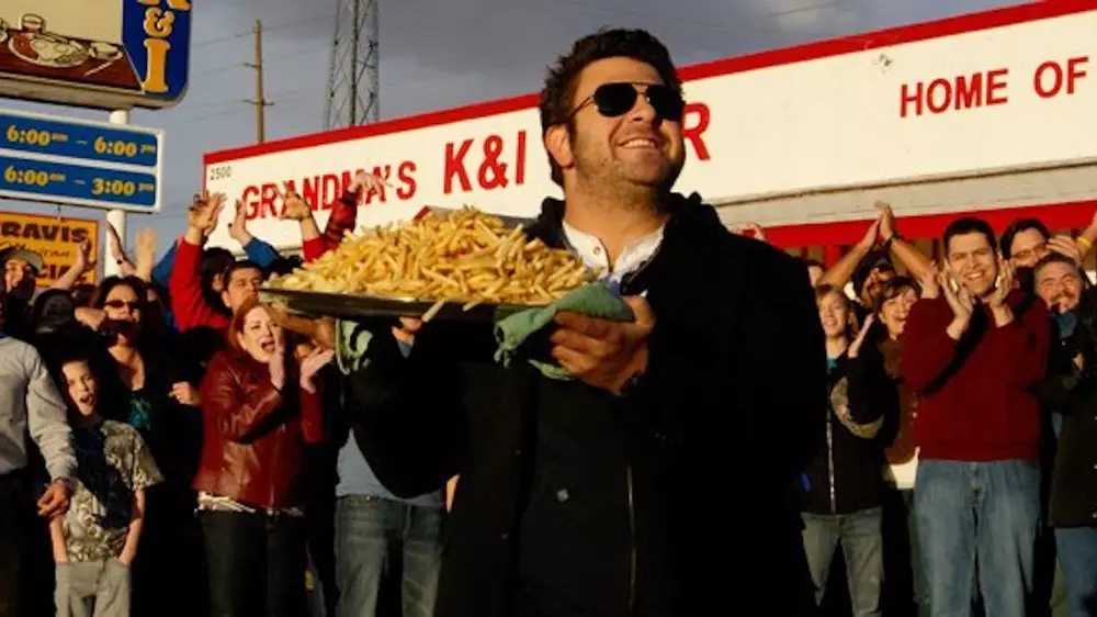 Adam Richman sosteniendo un plato de papas fritas frente a una multitud que vitoreaba