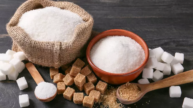 Verschiedene Zuckersorten, weiß granuliert und braun, in Bechern, Löffeln und Würfeln.