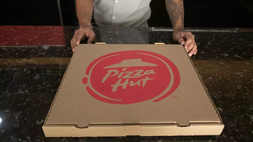 Handen duwen een Pizza Hut Pizzadoos naar voren