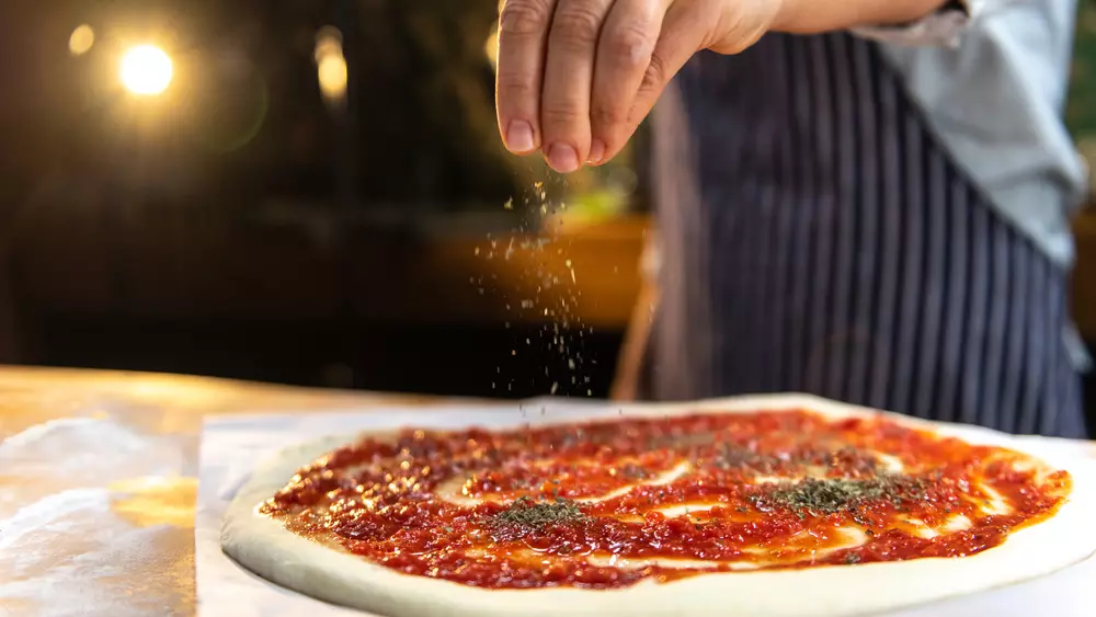 Lo chef cosparge di origano sulla pizza