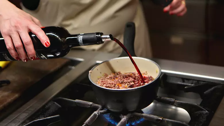 Vin hældes i en gryde med bolognese