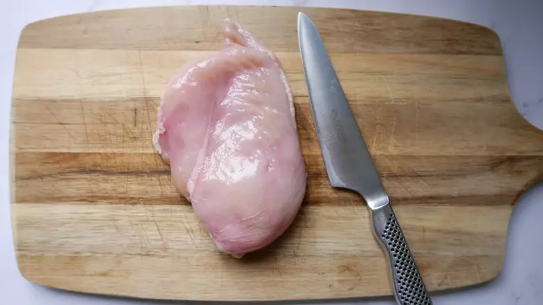 En kyllingebryst på et skærebræt med en kniv.