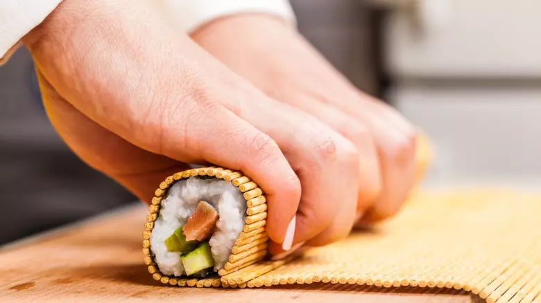 Primo piano delle mani che rotolano la stuoia di sushi